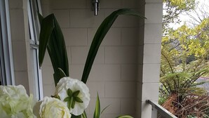 Uma varanda com uma mesa branca, uma planta em vaso e um vaso com flores brancas.