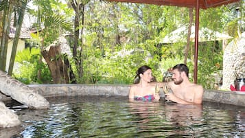 Um casal em uma piscina natural com parede de pedra e plantas tropicais.