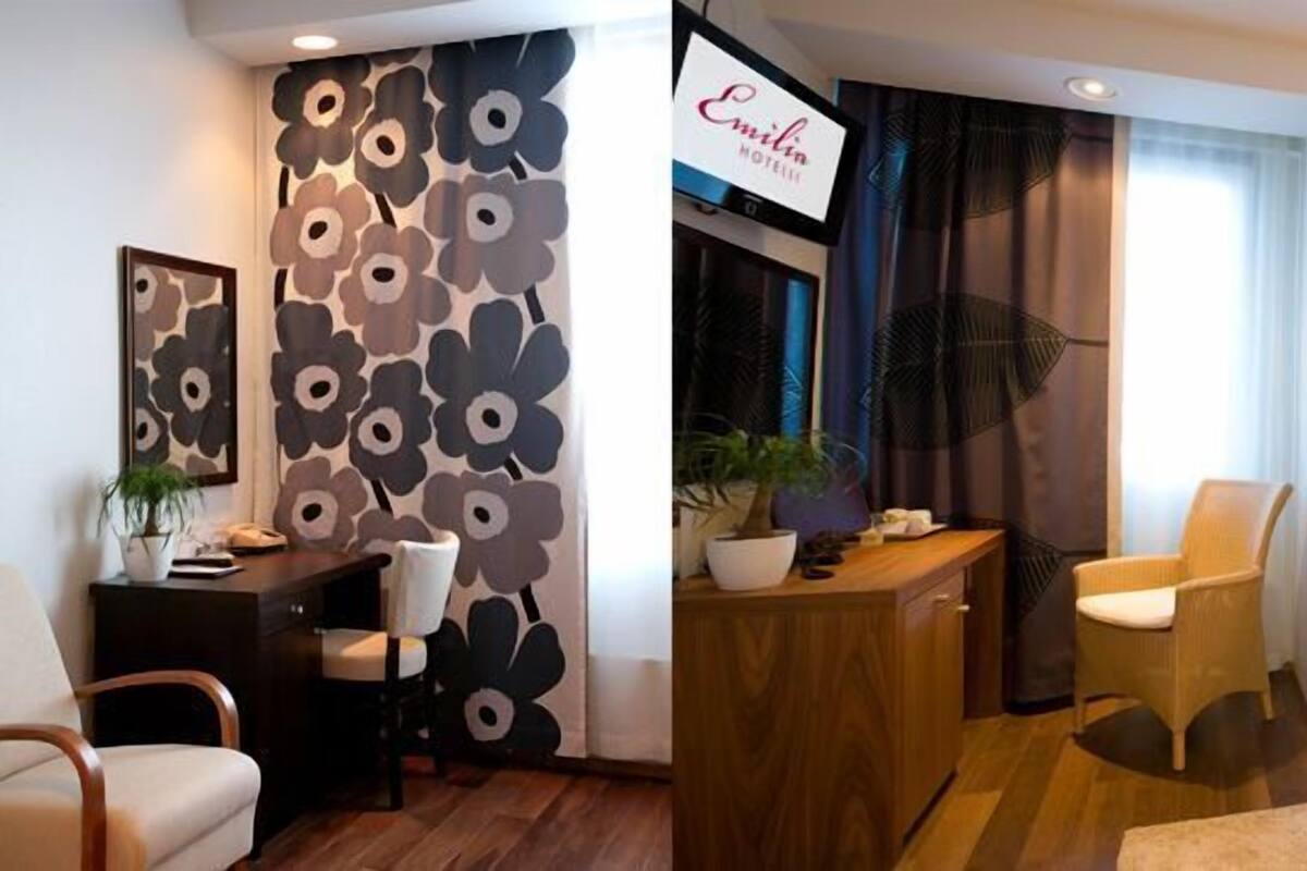 Quarto de hotel com cama, escrivaninha, cadeira, planta em vaso e televisão.