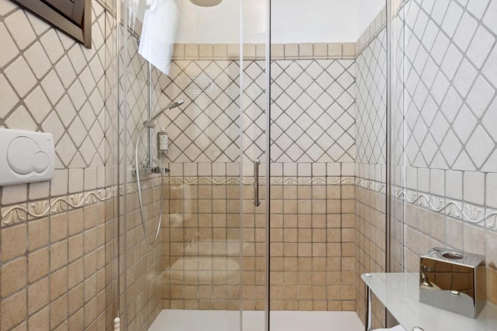Área de chuveiro com divisória de vidro, azulejos bege e um dispensador de toalhas.