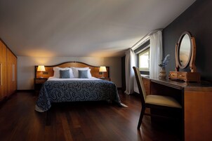 Quarto de hotel com uma cama grande, duas luminárias de cabeceira, uma escrivaninha de madeira com um espelho e uma cadeira.