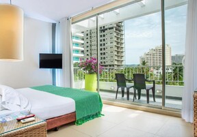 Quarto de hotel com cama, televisão, varanda com cadeiras e vista para edifícios.