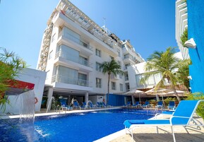 Um hotel com piscina, várias varandas e palmeiras.