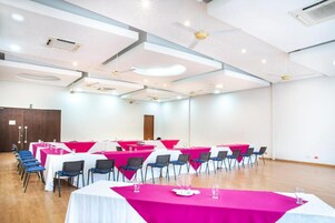 Uma sala de conferências com mesas e cadeiras, paredes brancas e ventiladores de teto.