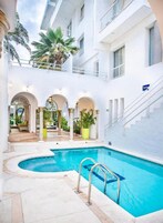 Uma piscina com design curvo, rodeada por paredes e colunas brancas, com uma escadaria que leva a um andar superior.