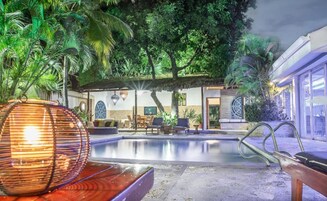 Área de piscina com espreguiçadeiras, espaço para refeições e área de estar coberta, tudo cercado por vegetação exuberante.