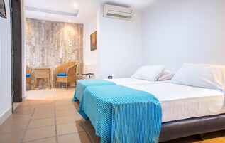 Quarto de hotel com uma cama, duas cadeiras, uma mesa pequena e uma parede com design texturizado.