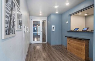Corredor com piso de madeira, balcão de recepção com computador e porta que dá para um quarto.
