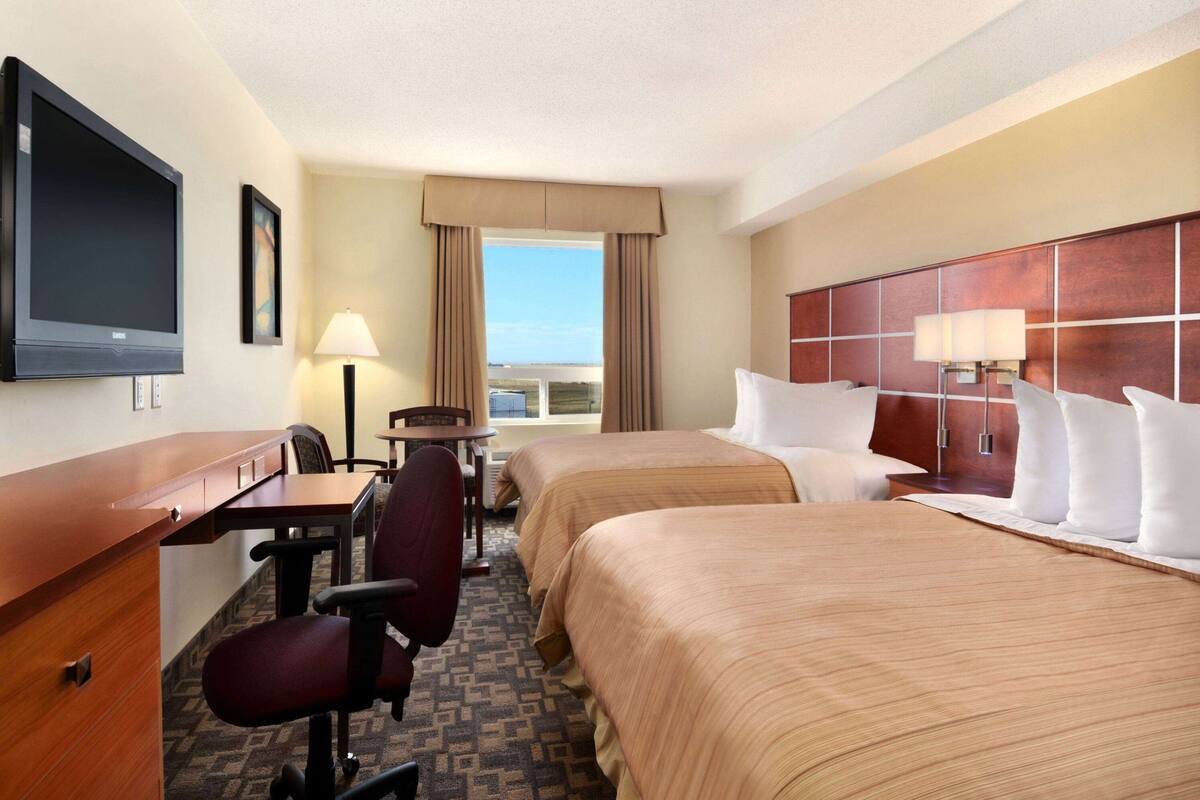 Quarto de hotel com duas camas, uma escrivaninha, uma cadeira, uma televisão e uma janela com cortinas.