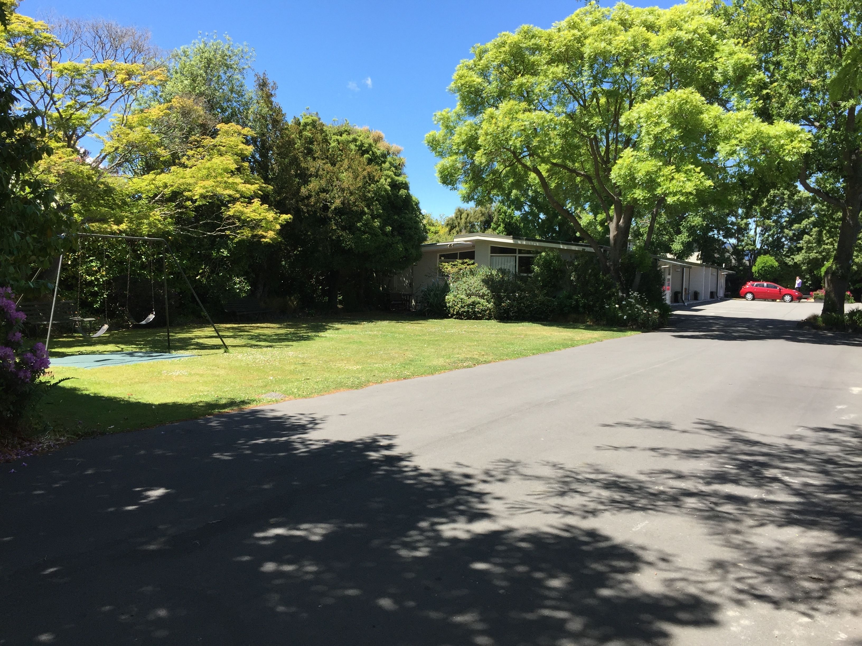 Uma entrada de casa residencial com balanço, um carro vermelho e uma casa com garagem.