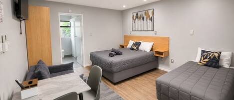 Quarto de hotel moderno com cama, escrivaninha, cadeira e mesa pequena.