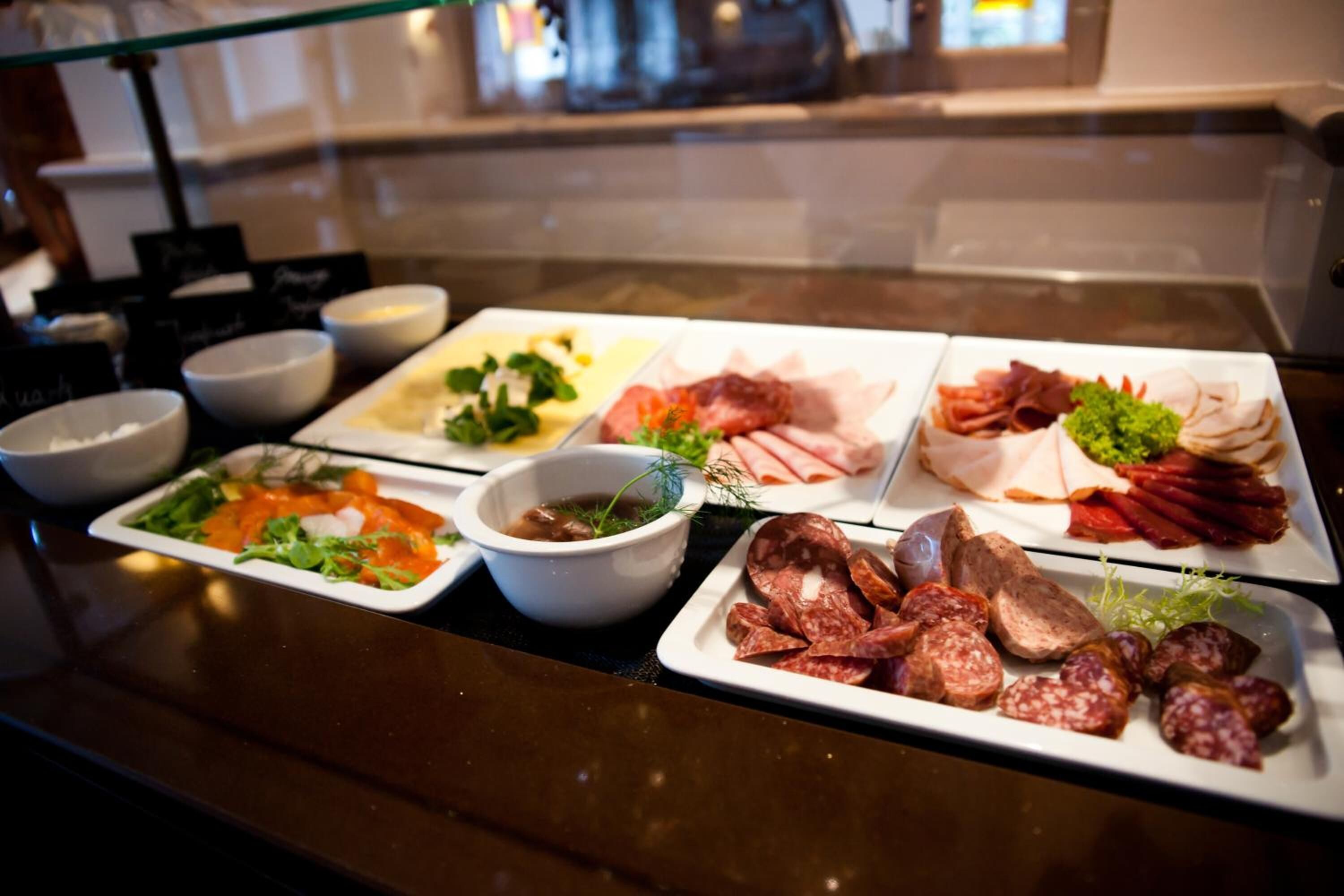 Buffet com diversos pratos, incluindo carnes, queijos e saladas.