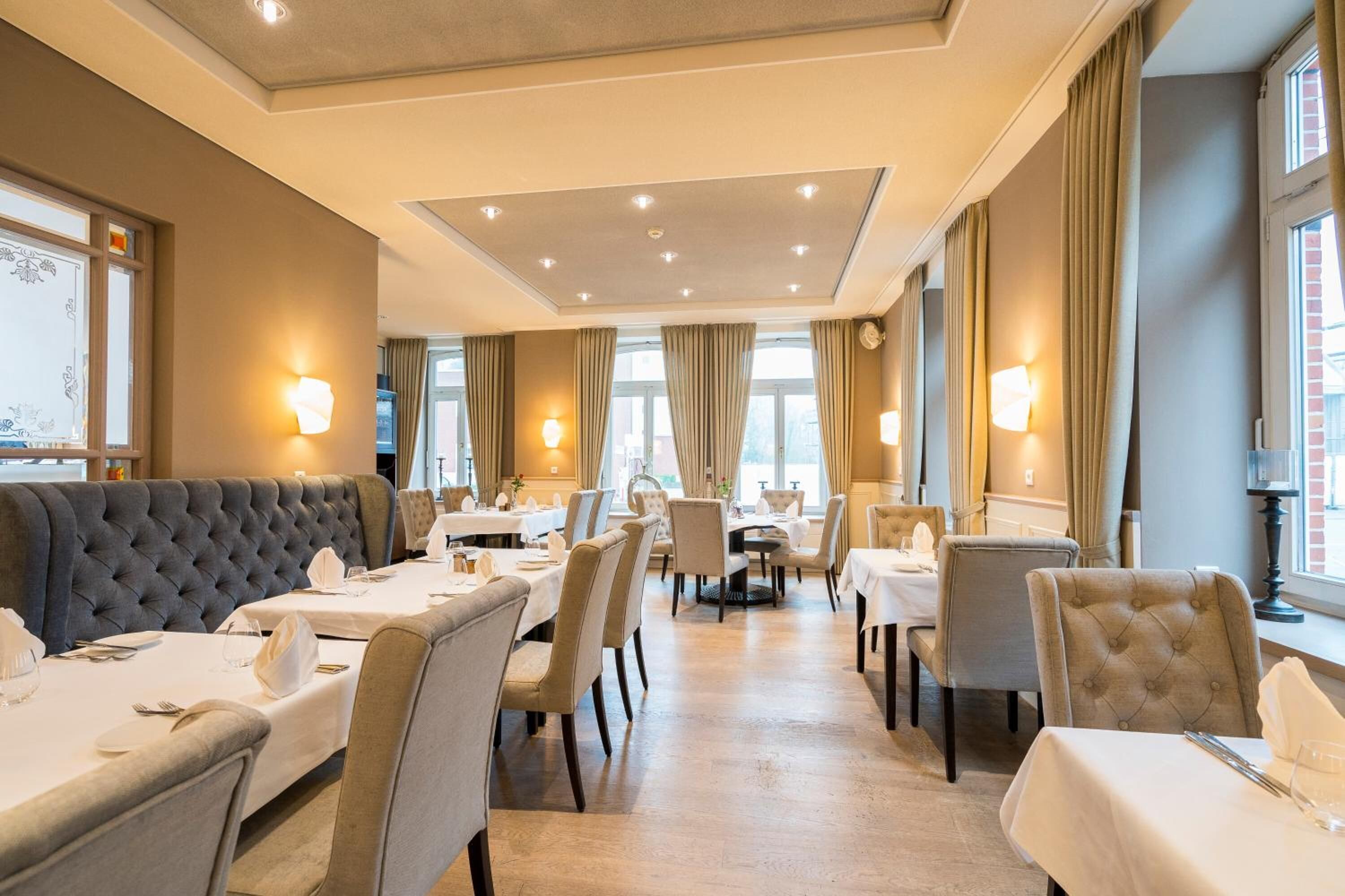 Uma sala de jantar de hotel com várias mesas e cadeiras, um sofá estofado e luminárias fixadas na parede.