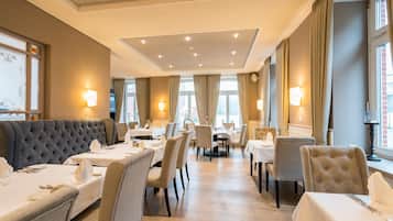 Uma sala de jantar de hotel com várias mesas e cadeiras, um sofá estofado e luminárias fixadas na parede.