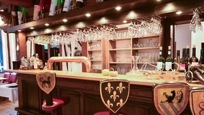 Uma área de bar com banquetas, prateleiras de garrafas e copos pendurados.