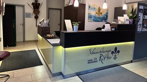 Balcão de recepção de hotel com uma placa indicando que é um hotel e restaurante. Há folhetos informativos e um vaso de planta sobre a mesa.