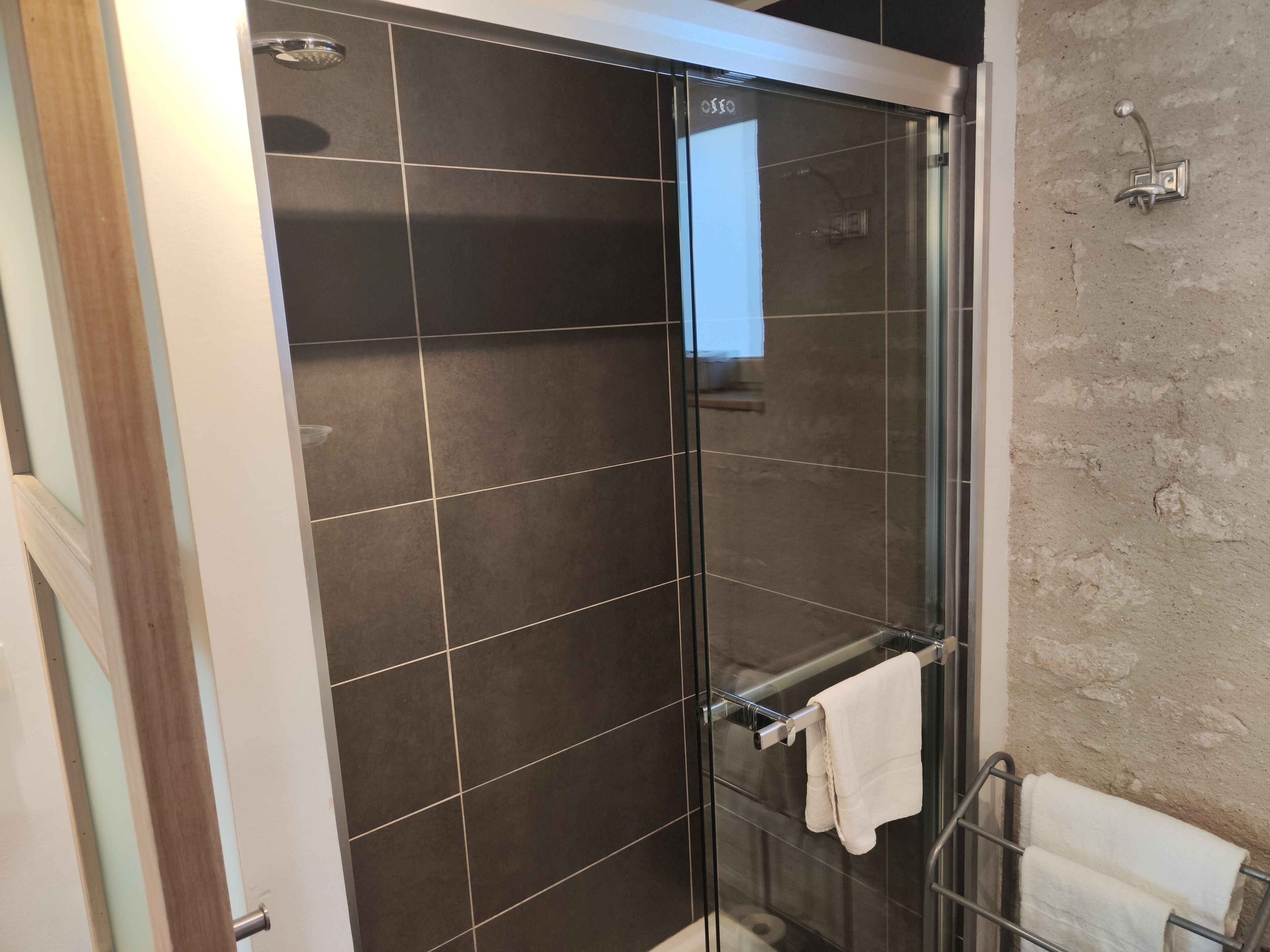Um banheiro moderno com paredes azulejadas escuras, box de vidro e porta-toalhas.