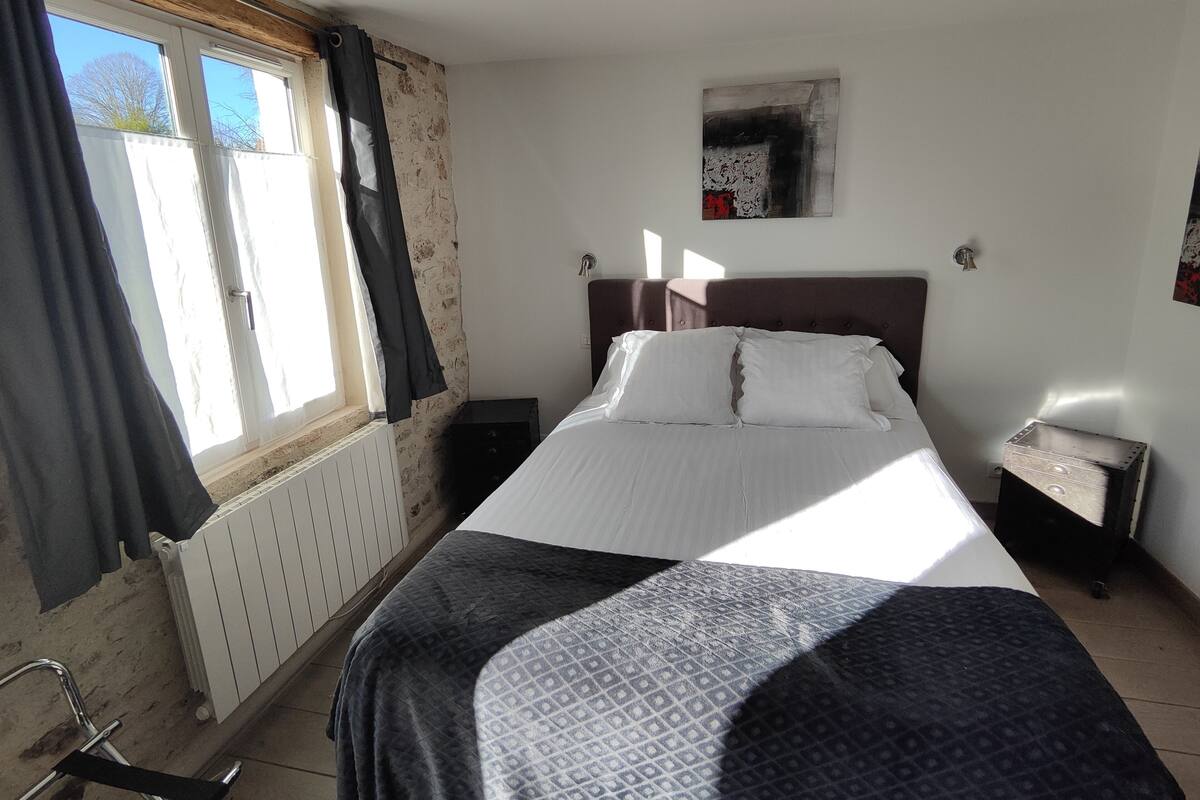 Quarto com cama, mesa de cabeceira, cômoda e janela com cortinas.