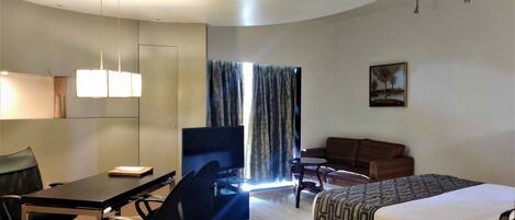 Quarto de hotel com escrivaninha, cadeira de escritório, cama e televisão.