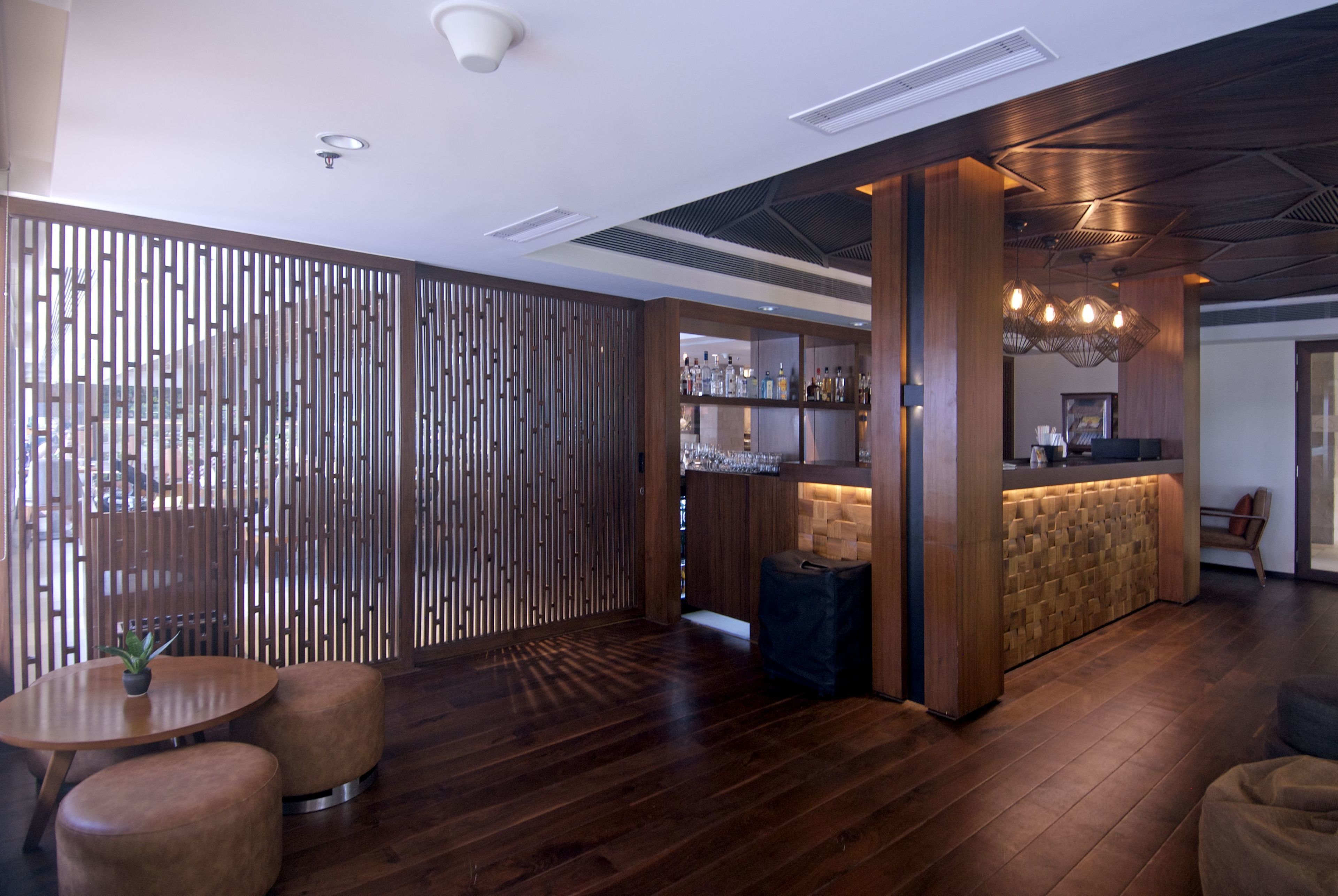 Uma área de bar moderna com painéis de madeira, balcão e espaço de estar com mesas redondas e pufes.