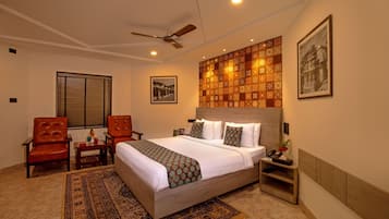 Quarto com cama, duas cadeiras, ventilador de teto, mesa de cabeceira e parede com azulejos estampados.