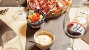 Uma mesa posta com uma tábua de frios, potes de patês e copos de vinho tinto.