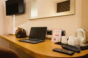 Uma receção de hotel com um laptop, um comando, uma máquina de café e um sinal que indica quarto para não fumadores.