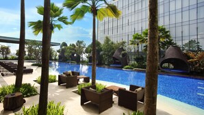 Uma área de piscina moderna de hotel, com espreguiçadeiras, uma piscina grande e altas palmeiras.