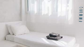 Quarto minimalista com uma cama branca, uma mesa pequena e uma janela com cortinas finas.