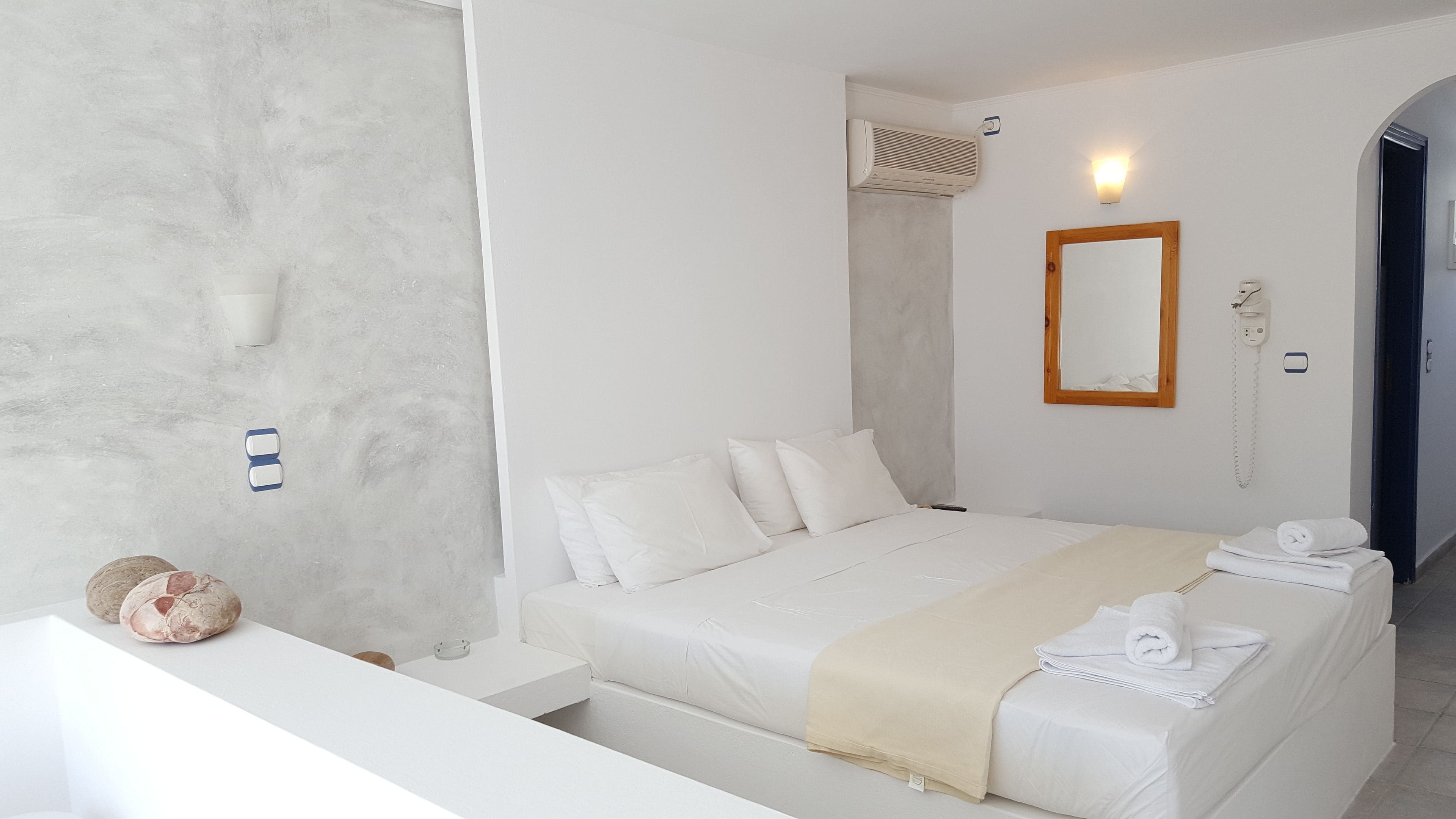 Quarto de hotel com cama, mesa de cabeceira, espelho, telefone e banheiro com banheira.