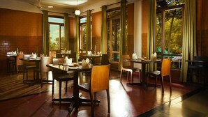 Restaurante com paredes de tijolo, janelas amplas e mobiliário de madeira. Mesas montadas com pratos, copos e guardanapos.