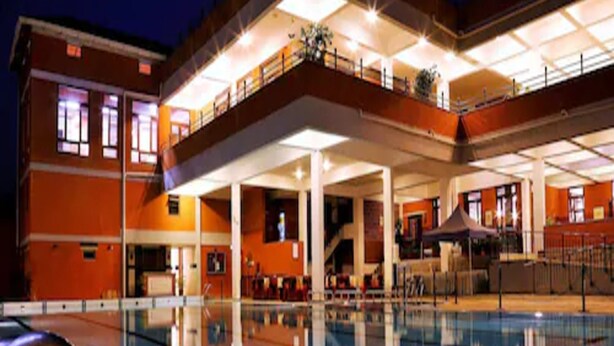 Um hotel com piscina, vários andares e área externa coberta.