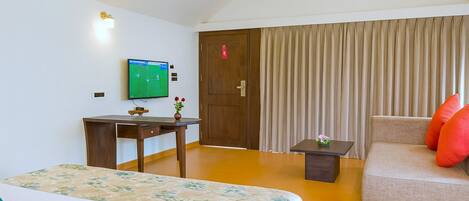 Quarto de hotel com cama, escrivaninha, sofá, televisão e porta.