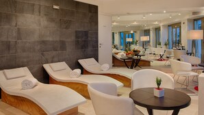 Uma área de spa moderna com cadeiras reclináveis, uma pequena mesa com uma planta e um espelho refletindo o espaço.