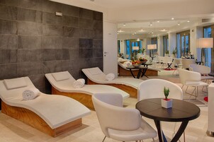 Uma área de spa moderna com cadeiras reclináveis, uma pequena mesa com uma planta e um espelho refletindo o espaço.