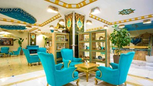 Um lobby com poltronas turquesa, uma mesa central e espelhos decorativos.