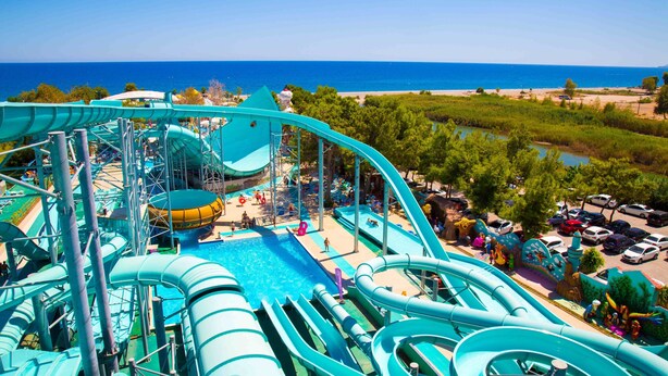 Parque aquático com vários toboáguas e área de piscina, com vista para uma praia e oceano.