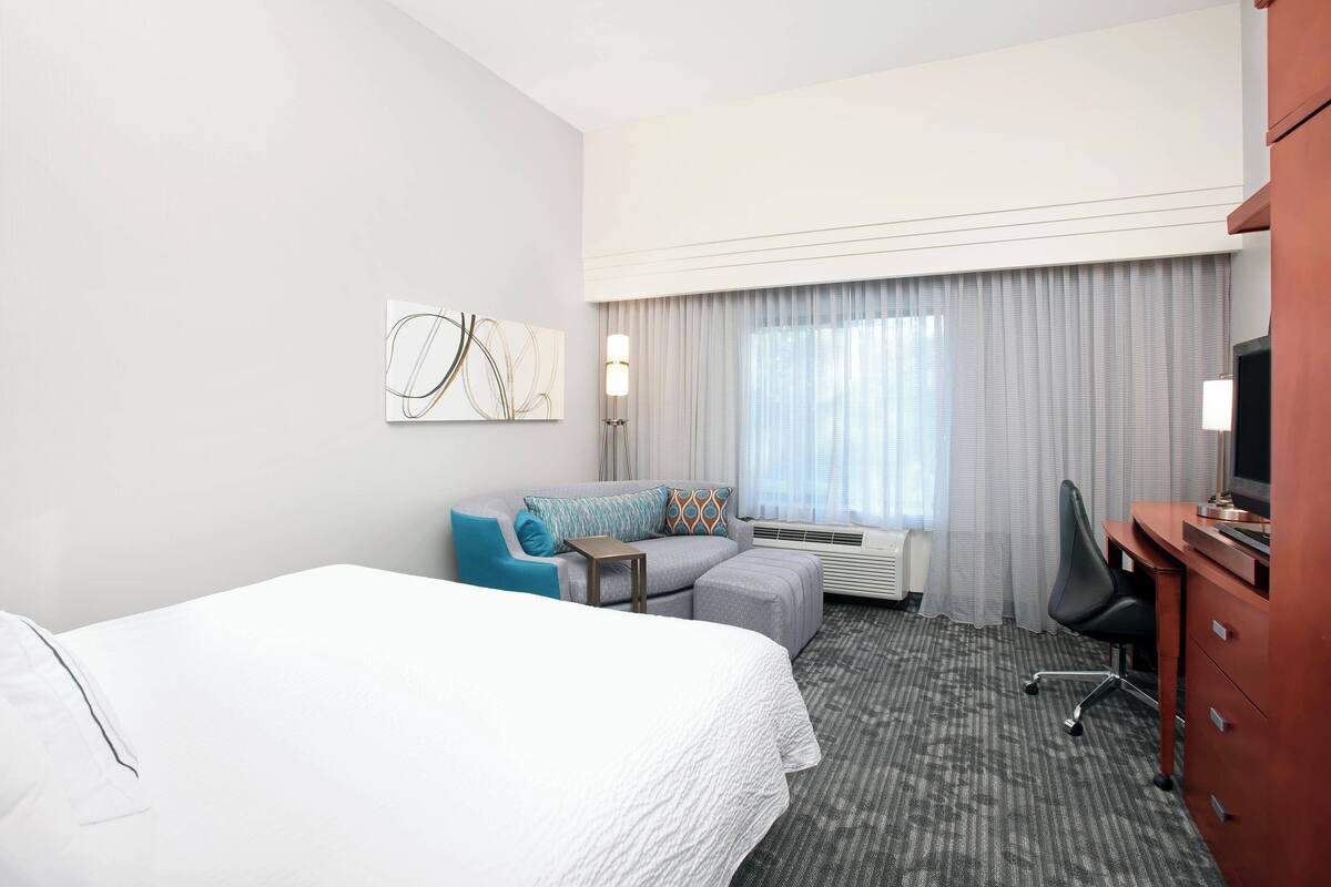 Quarto de hotel com cama, sofá, escrivaninha e televisão.