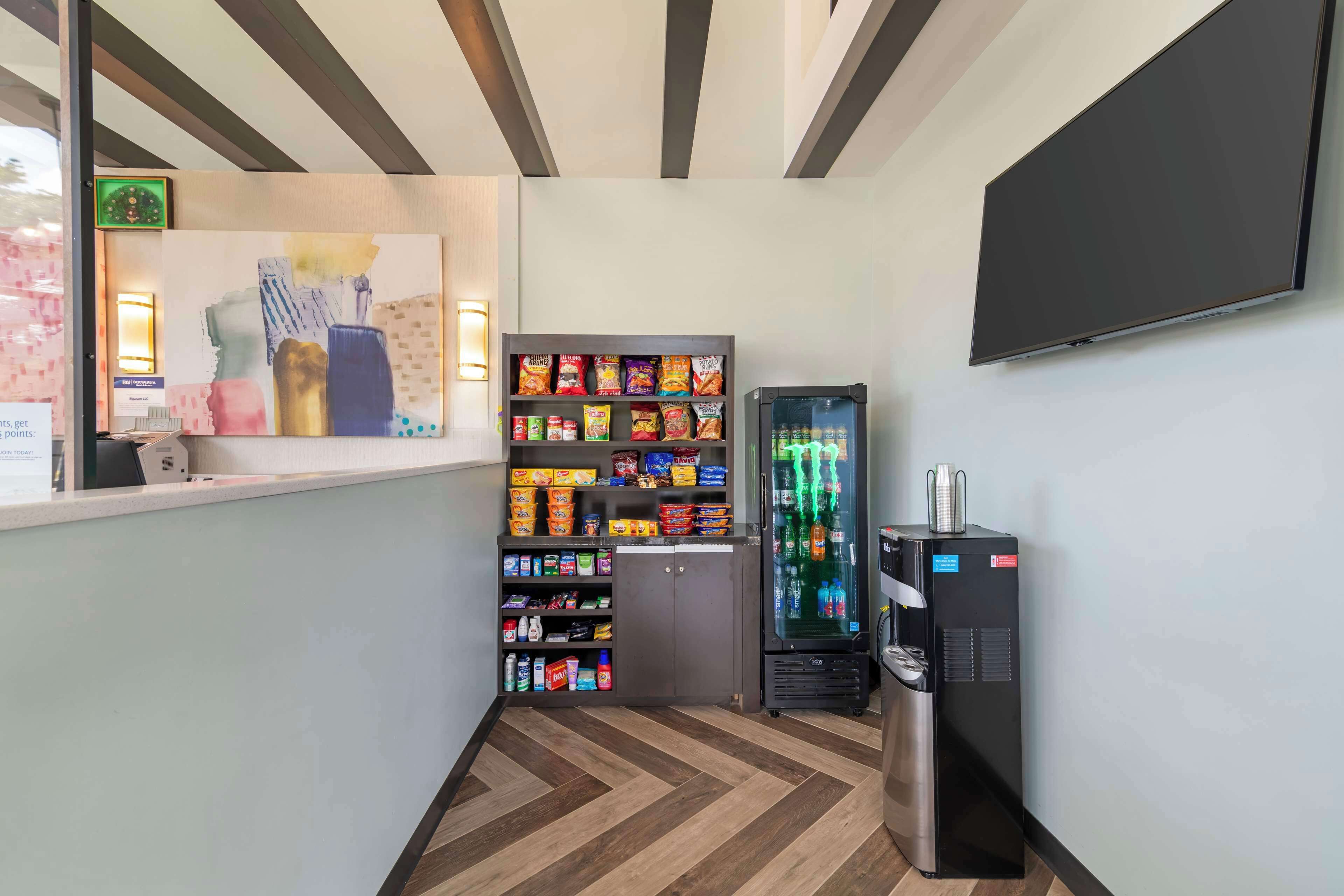 Uma área de recepção com balcão, dispensador de bebidas e prateleira com lanches.