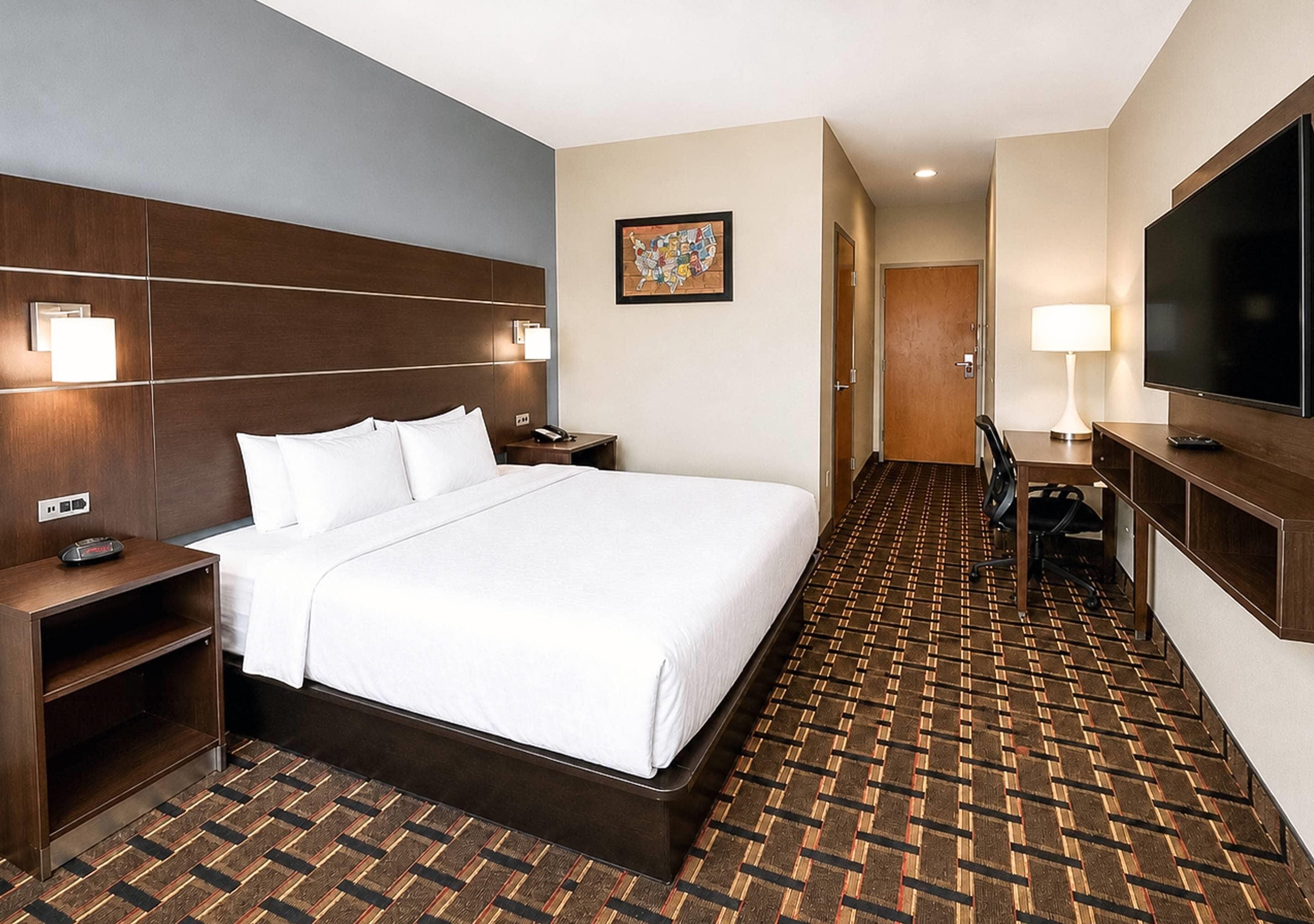 Quarto de hotel com uma cama grande, mesas de cabeceira, televisão e um chão estampado.