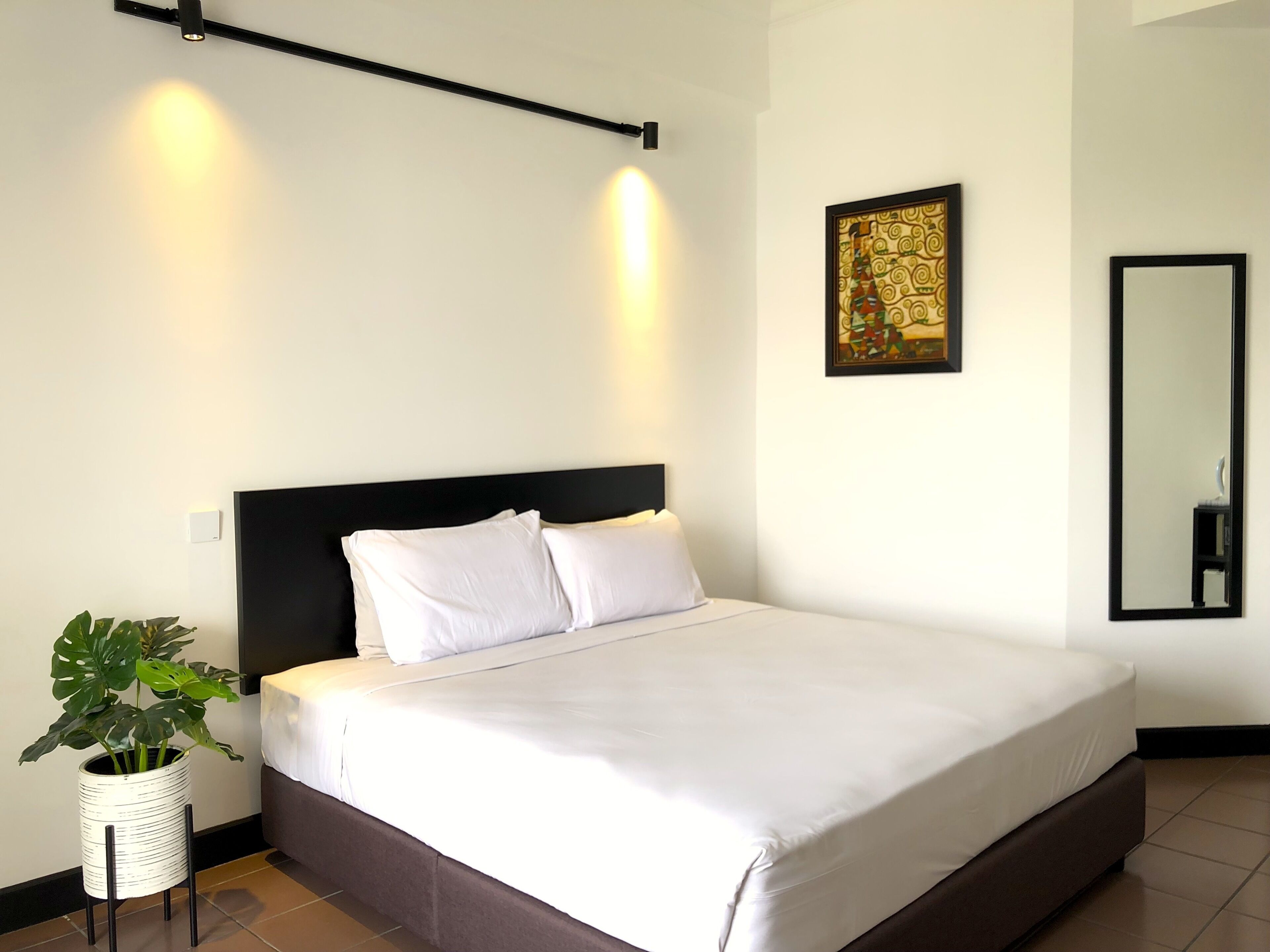Quarto de hotel moderno com uma cama grande, um vaso de planta, uma obra de arte emoldurada e um espelho.