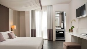 Quarto de hotel com uma cama grande, uma escrivaninha, televisão e banheiro visível através de uma porta.