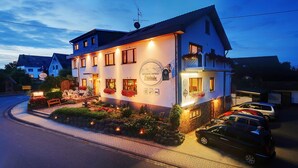 Um edifício de dois andares com um letreiro de restaurante, área externa para clientes e carros estacionados.