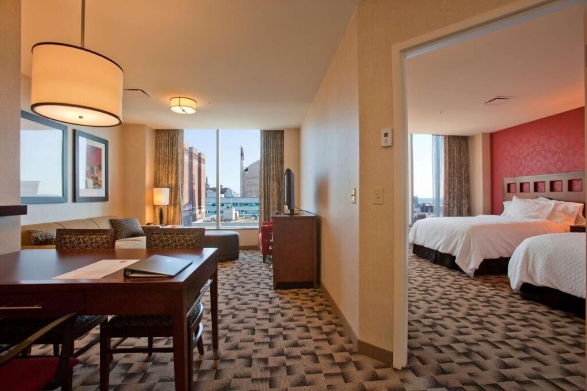 Quarto de hotel com escrivaninha, duas camas, vista para a cidade e carpete estampado.