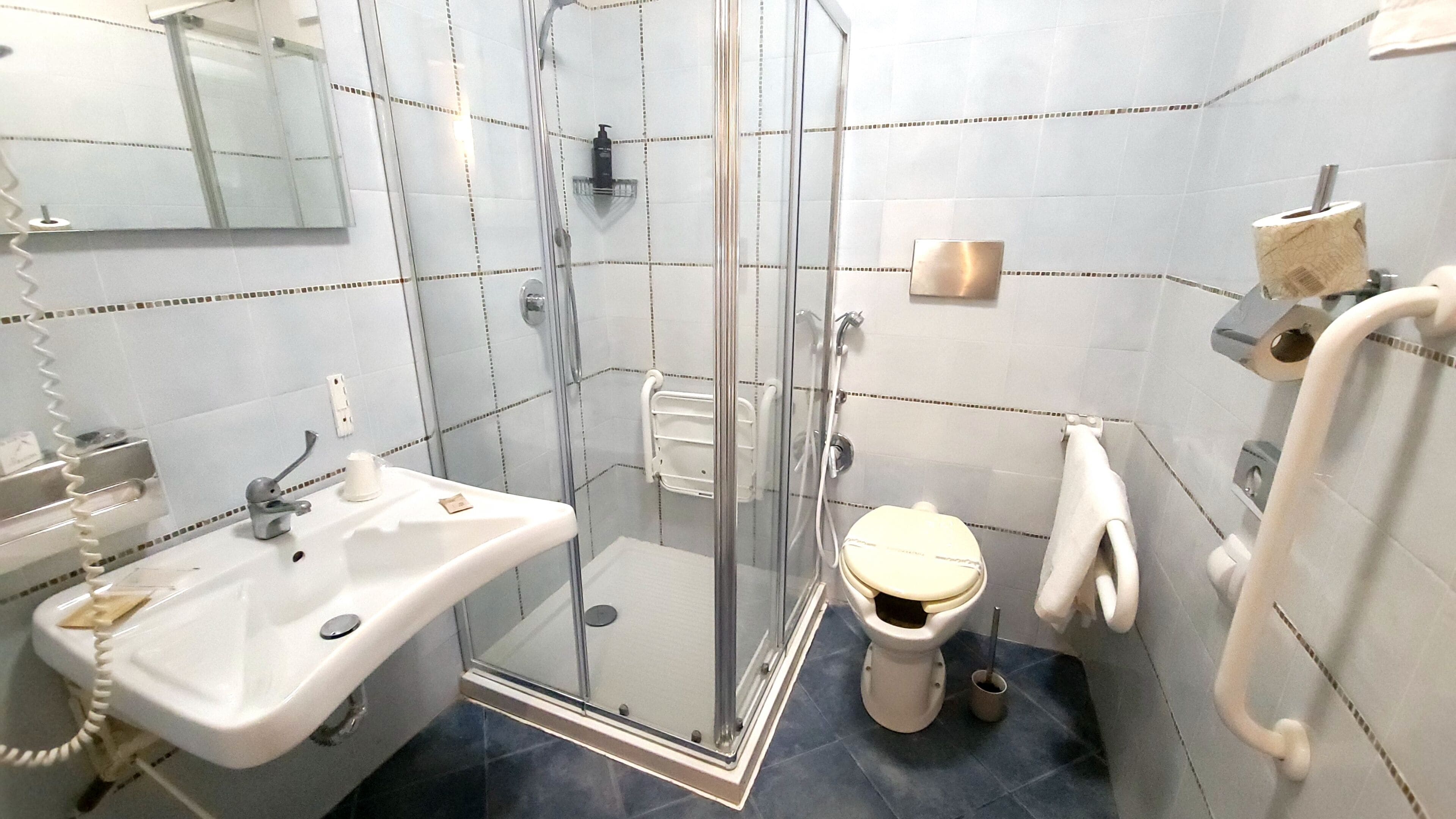 Casa de banho com cabine de duche em vidro, uma pia, sanita e um porta-toalhas.