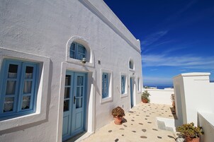 Um edifício branco com portas e janelas azuis, um pátio com azulejos e plantas em vasos.