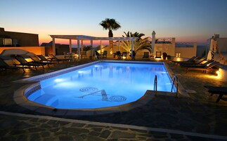 Piscina com padrão geométrico, cercada por espreguiçadeiras e uma pérgola, ao pôr do sol.