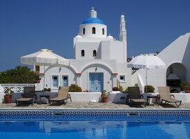 Um edifício branco com cúpulas azuis e área de piscina com espreguiçadeiras.