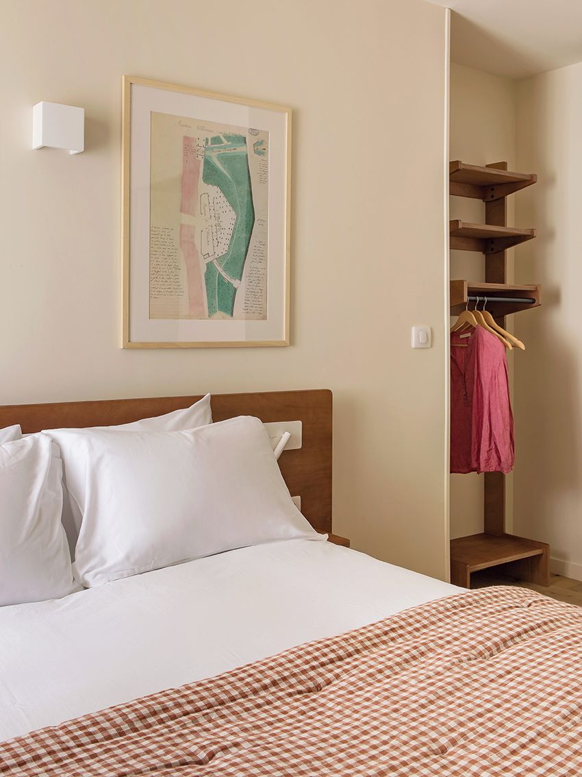 Uma cama bem arrumada com lençóis brancos, um mapa emoldurado na parede e uma prateleira de madeira com cabides.