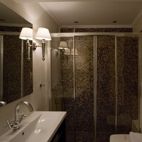 Casa de banho com cabine de chuveiro em vidro, lavatório com espelho e candeeiros de parede.
